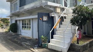 Um edifício de dois andares com varanda, escada e placa indicando que o imóvel está à venda.