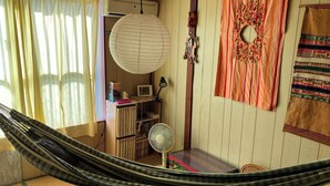 Quarto com rede, ventoinha, escrivaninha e computador, e parede decorada.