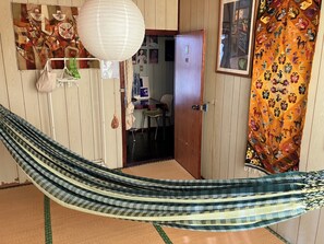 Quarto com rede, paredes de madeira, uma porta, uma cadeira e cortina estampada.