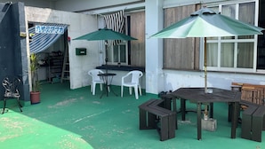 Área de pátio externo com mesa e cadeiras, um guarda-sol verde e uma placa com caracteres japoneses.