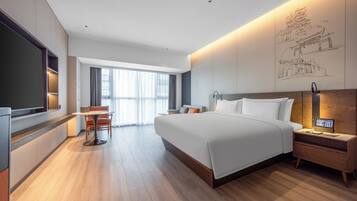Quarto de hotel moderno com uma cama grande, mesas de cabeceira, escrivaninha e televisão.