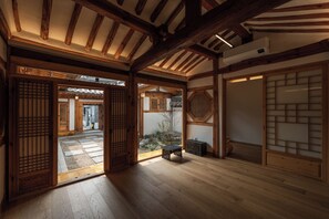 Um interior japonês tradicional com tatames, vigas de madeira, portas deslizantes e vista para um jardim de pedras.