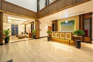 Uma área de recepção de hotel com design moderno, incluindo um balcão de atendimento, espaço de estar e plantas em vasos.