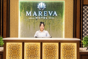 Uma receção de hotel com o letreiro 'MAREVA HOTEL' e um recepcionista.