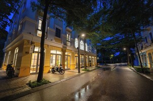 Vista da rua à noite, com um edifício com grandes janelas e uma scooter estacionada.