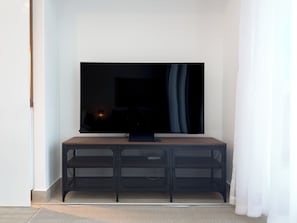 Uma sala de estar moderna com uma televisão de tela plana presa a um armário de metal preto, piso de madeira e parede branca.