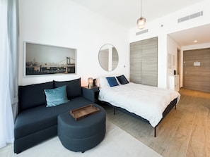Quarto moderno com cama, sofá, puf redondo, mesa de cabeceira com luminária, espelho e uma grande moldura com imagem na parede.