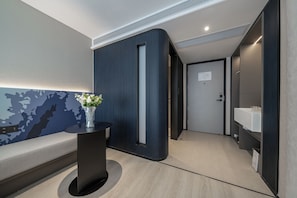 Um saguão de hotel moderno com área de estar, balcão de recepção e um banheiro visível ao fundo.