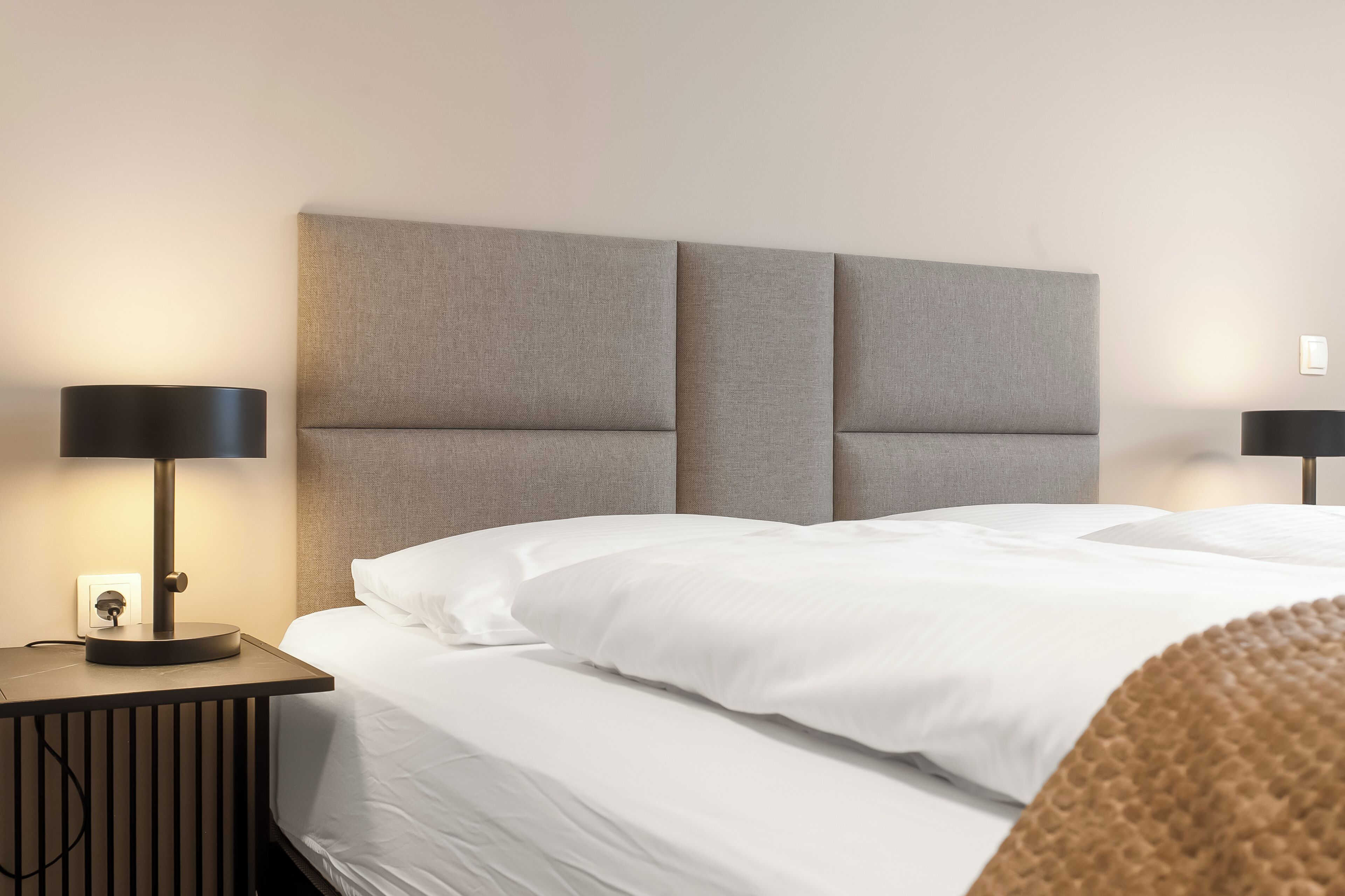 Quarto de hotel moderno com uma cama grande, duas mesas de cabeceira com luminárias e uma paleta de cores neutras.