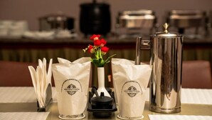 Uma mesa com um conjunto de chá, um vaso com flores vermelhas e duas sacolas com um logotipo.