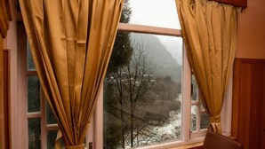 Quarto com janela, cortinas, uma cadeira e vista para uma paisagem montanhosa.