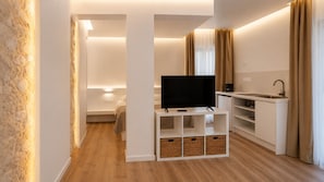 Uma sala de estar moderna com televisão de tela plana, área de cozinha com pia e armários, e um espaço de estar aconchegante com uma cama.