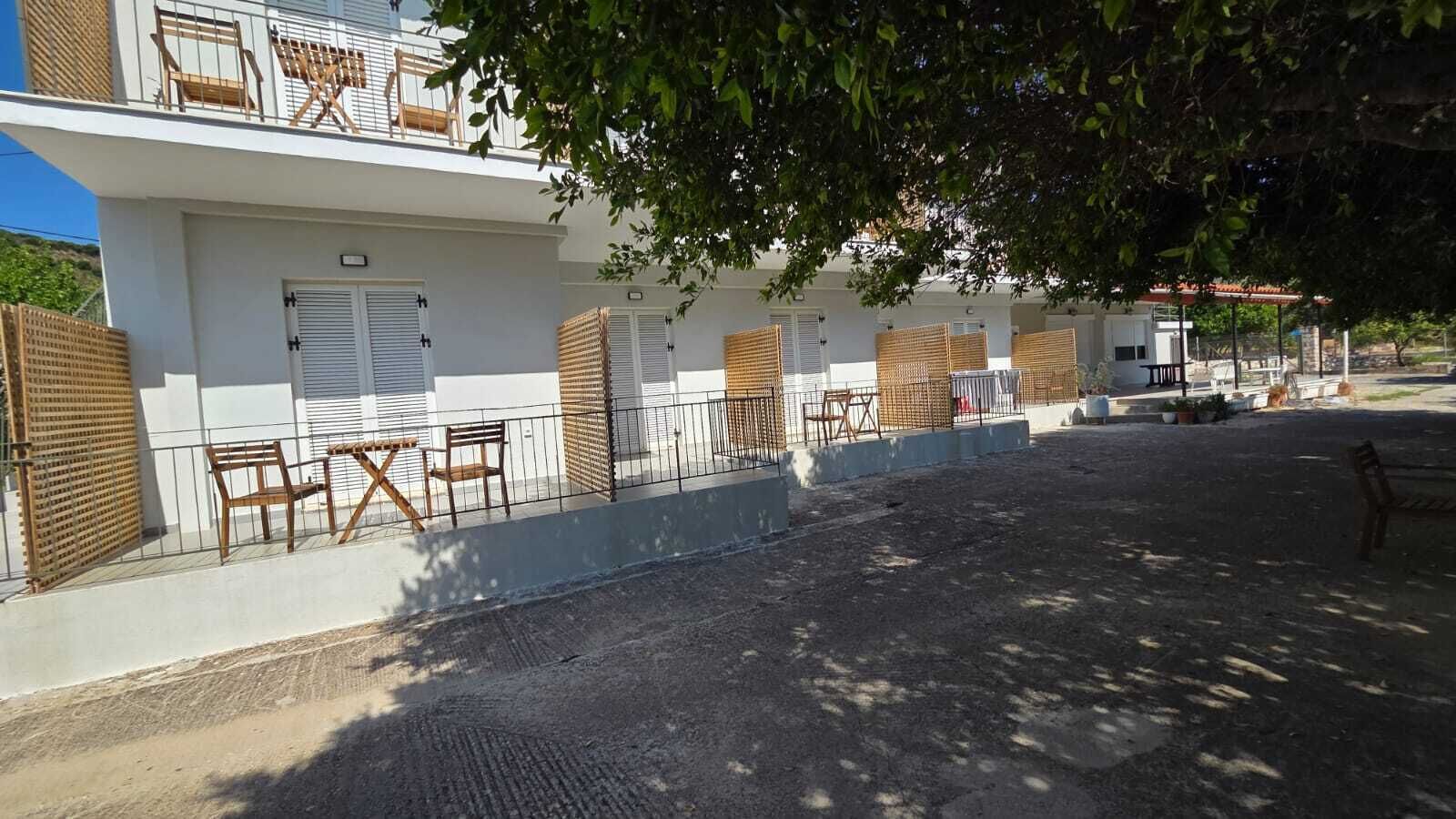 Uma fileira de edifícios brancos com varandas, mesas ao ar livre e um espaço pavimentado.