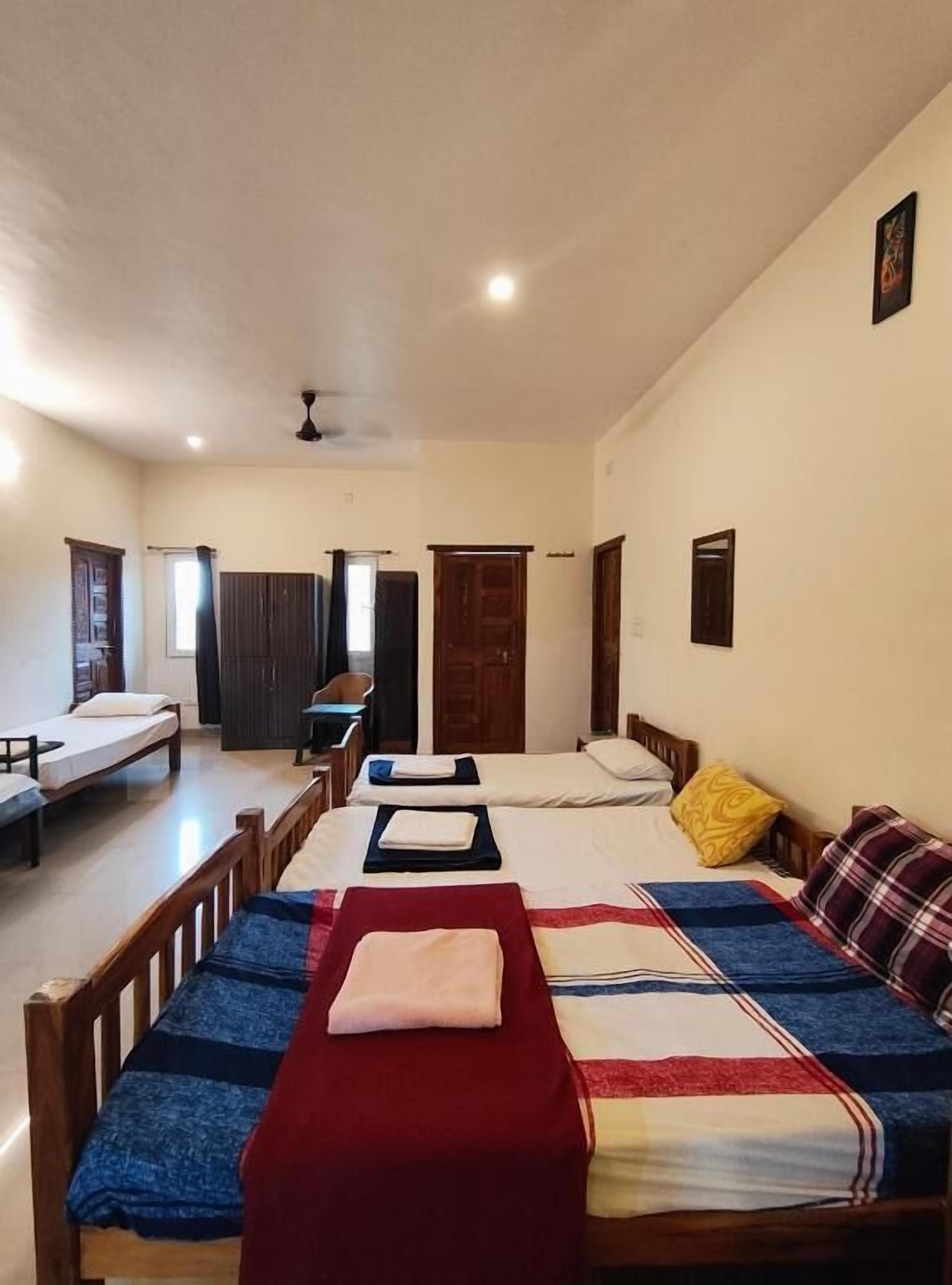 Quarto de hotel com duas camas, um sofá, um banco de madeira e um ventilador de teto.
