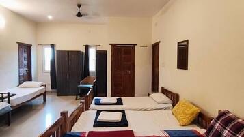 Quarto de hotel com duas camas, um sofá, um banco de madeira e um ventilador de teto.