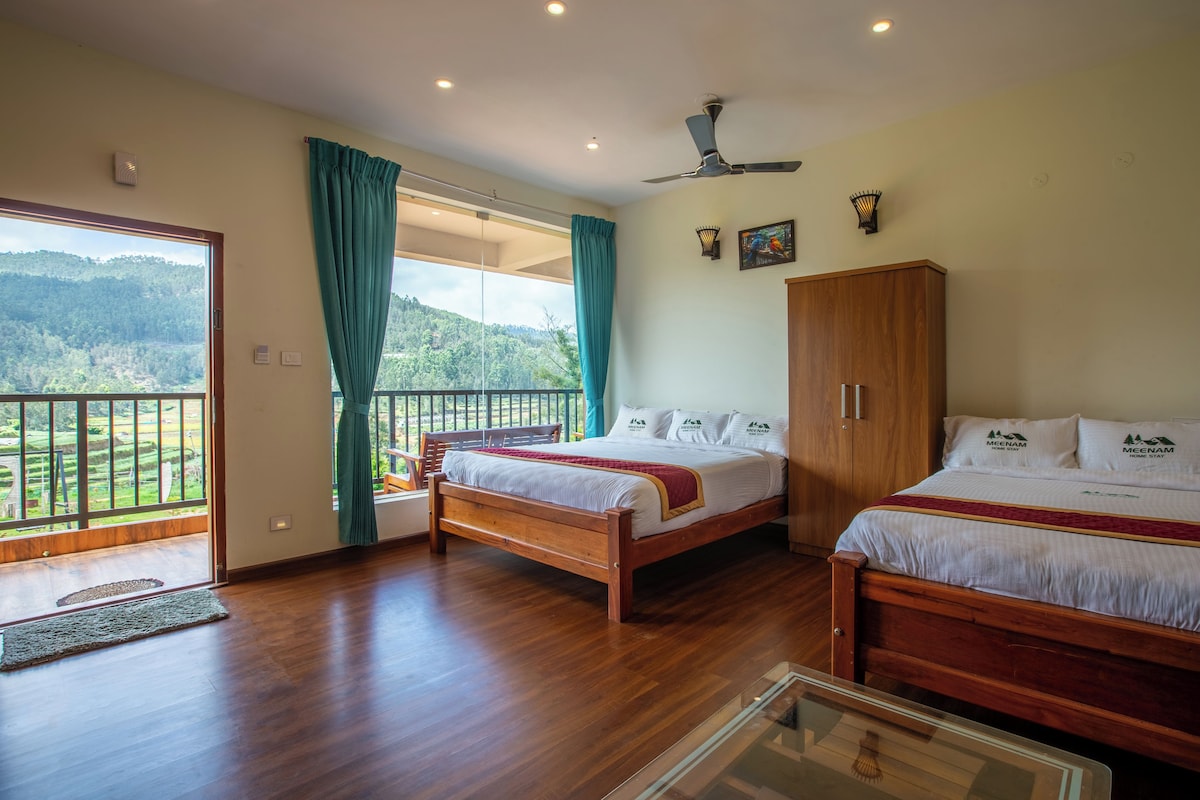 Quarto de hotel com duas camas, guarda-roupa de madeira, varanda com vista para as colinas e ventoinha no teto.