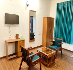 Quarto com escrivaninha de madeira, duas cadeiras, televisão, guarda-roupa e janela com cortinas.