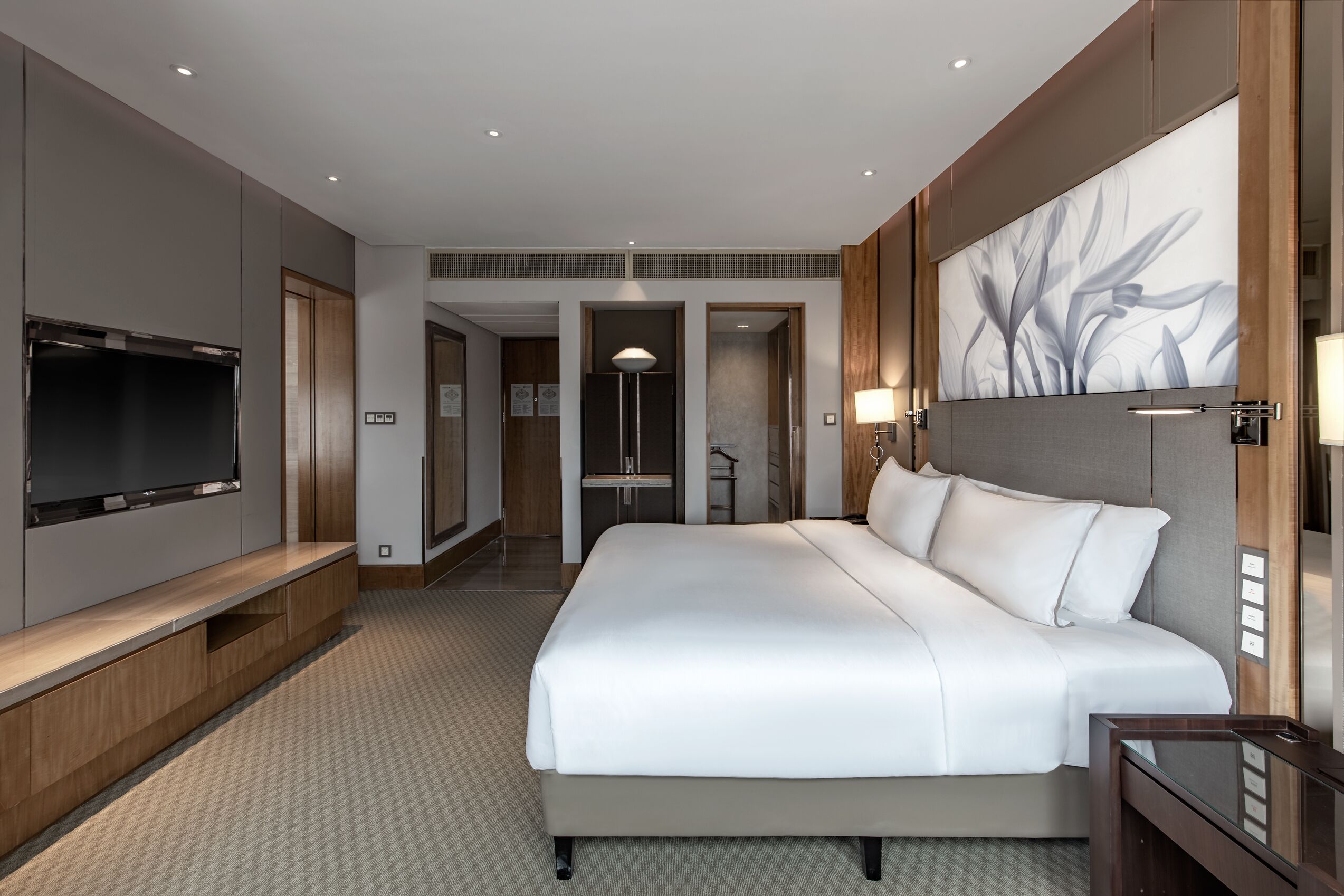 Quarto de hotel com uma cama grande, televisão de tela plana, escrivaninha e luminária de parede.