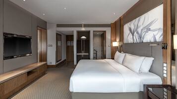 Quarto de hotel com uma cama grande, televisão de tela plana, escrivaninha e luminária de parede.