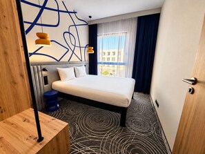 Quarto de hotel com cama, escrivaninha e vista para a cidade.