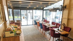 Restaurante com buffet, mesas de madeira e cadeiras vermelhas.
