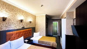 Quarto de hotel com duas camas, televisão, minibar e casa de banho visível através de uma porta.