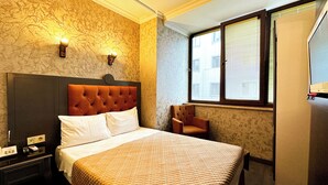 Quarto de hotel com uma cama grande, mesa de cabeceira, cadeira e janela com persianas.