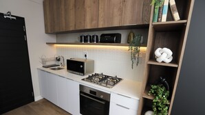 Uma cozinha moderna com armários brancos, fogão a gás, micro-ondas e uma estante com livros e objetos decorativos.