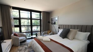 Quarto de hotel com uma cama grande, um sofá, uma mesa e vista para o exterior através de uma janela ampla.