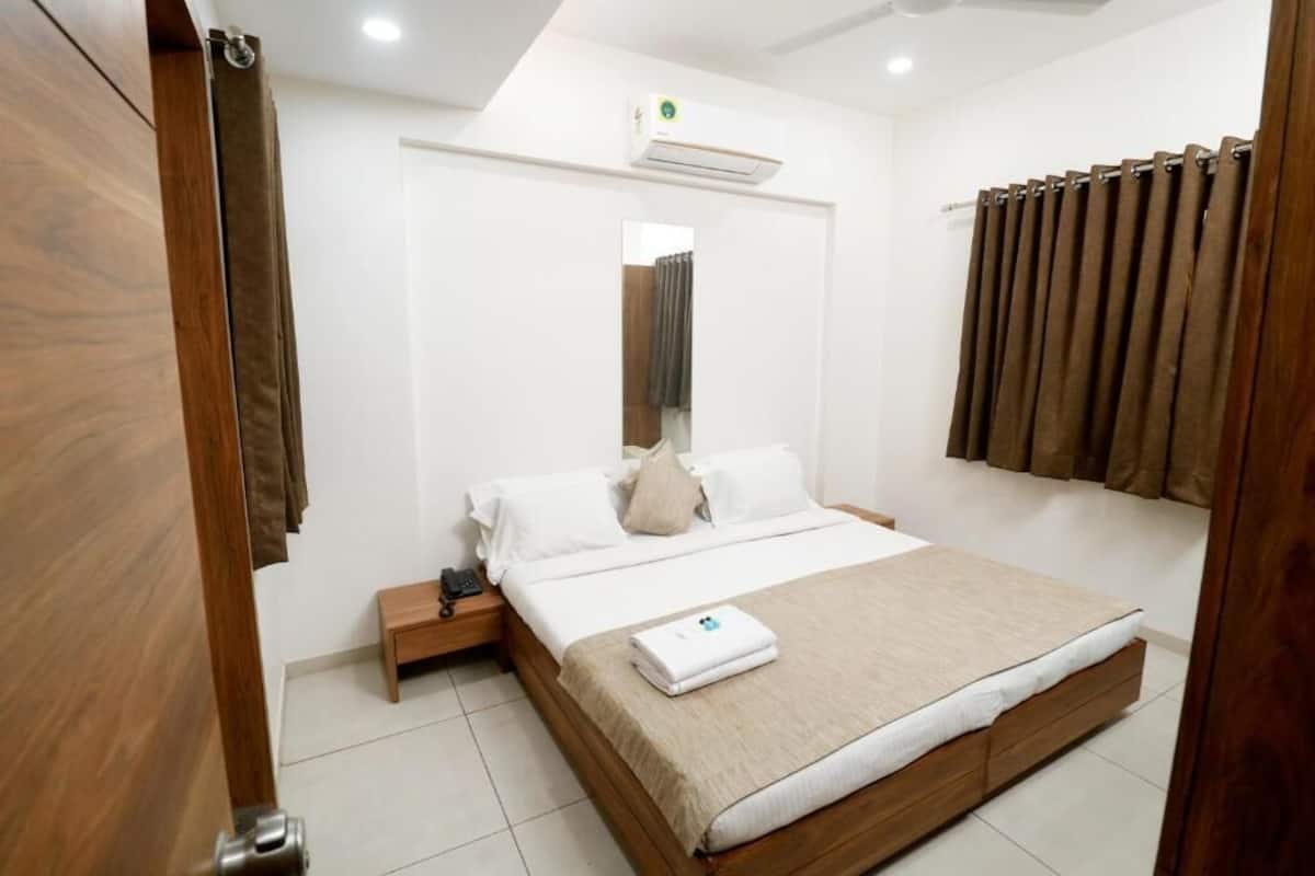 Quarto com cama, mesa de cabeceira, ar condicionado fixado na parede e janela com cortinas.