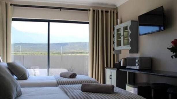 Quarto de hotel com duas camas, televisão, escrivaninha e vista para a paisagem.