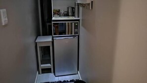 Cozinha compacta com geladeira, micro-ondas e um balcão pequeno.