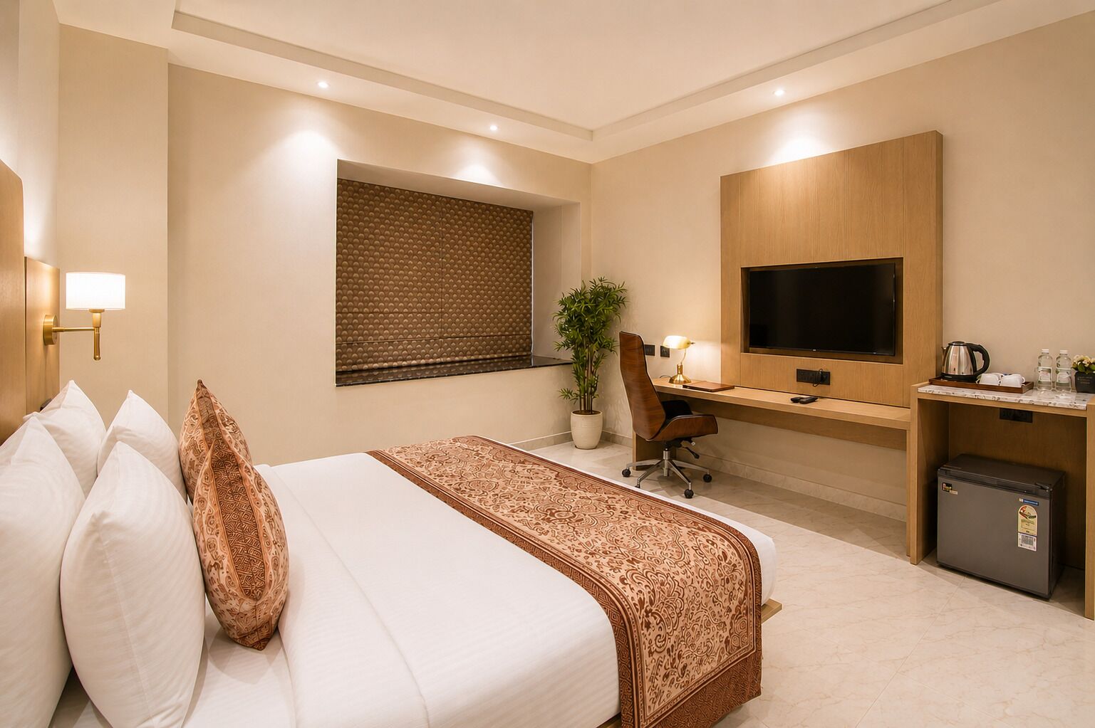 Quarto de hotel com cama, escrivaninha, televisão e um pequeno frigorífico.