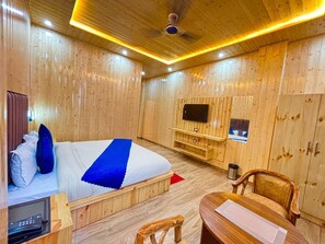 Quarto de madeira com uma cama, uma televisão presa à parede, uma escrivaninha e uma cadeira.