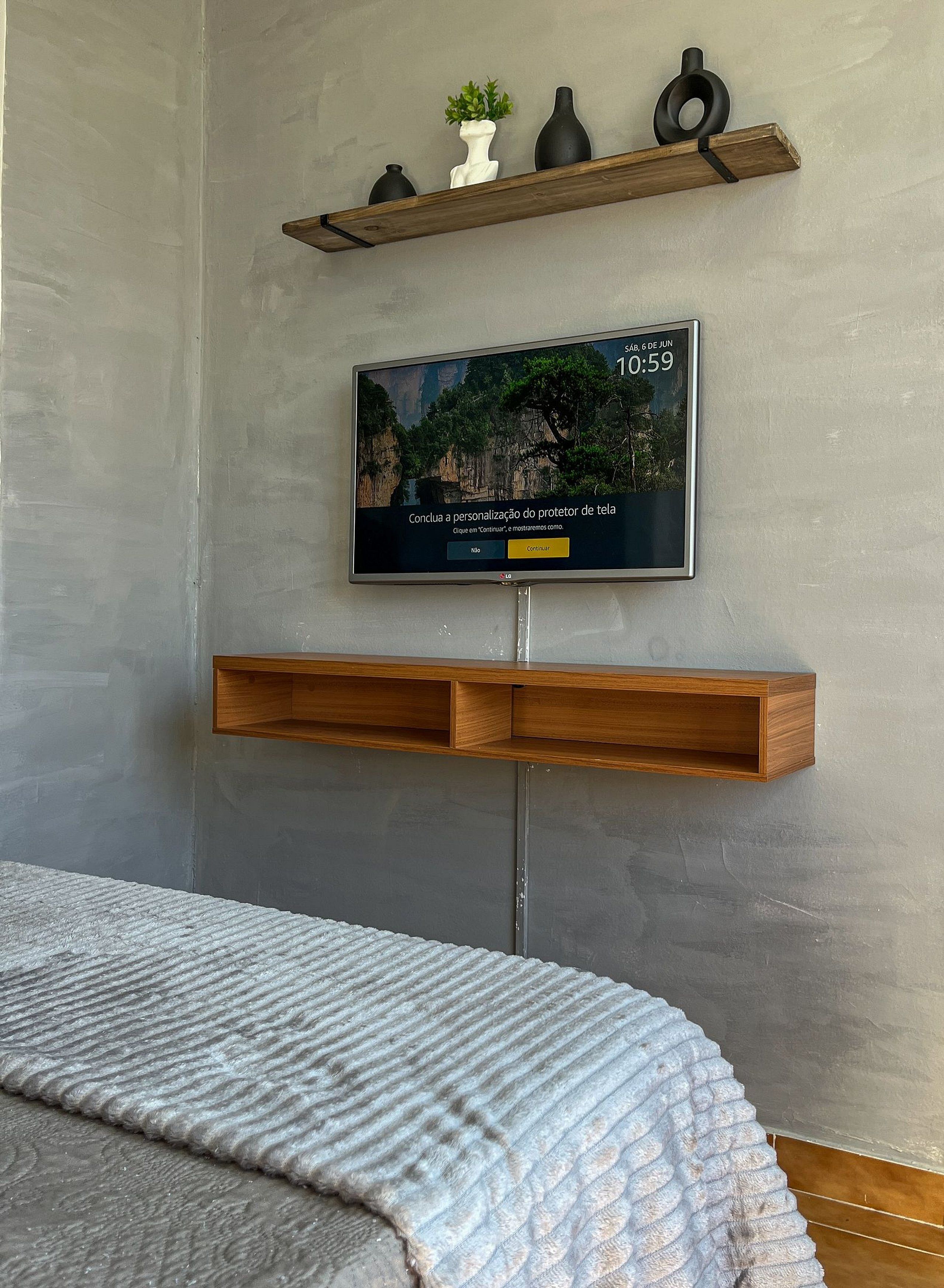 Um quarto com uma cama, uma televisão montada e uma prateleira de madeira acima da cama.