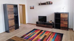 Uma sala de estar moderna com televisão de tela plana, armários de madeira, tapete colorido e luminária pendente.
