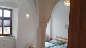 Quarto com cama de madeira, radiador, janela com persianas e luminária pendente.