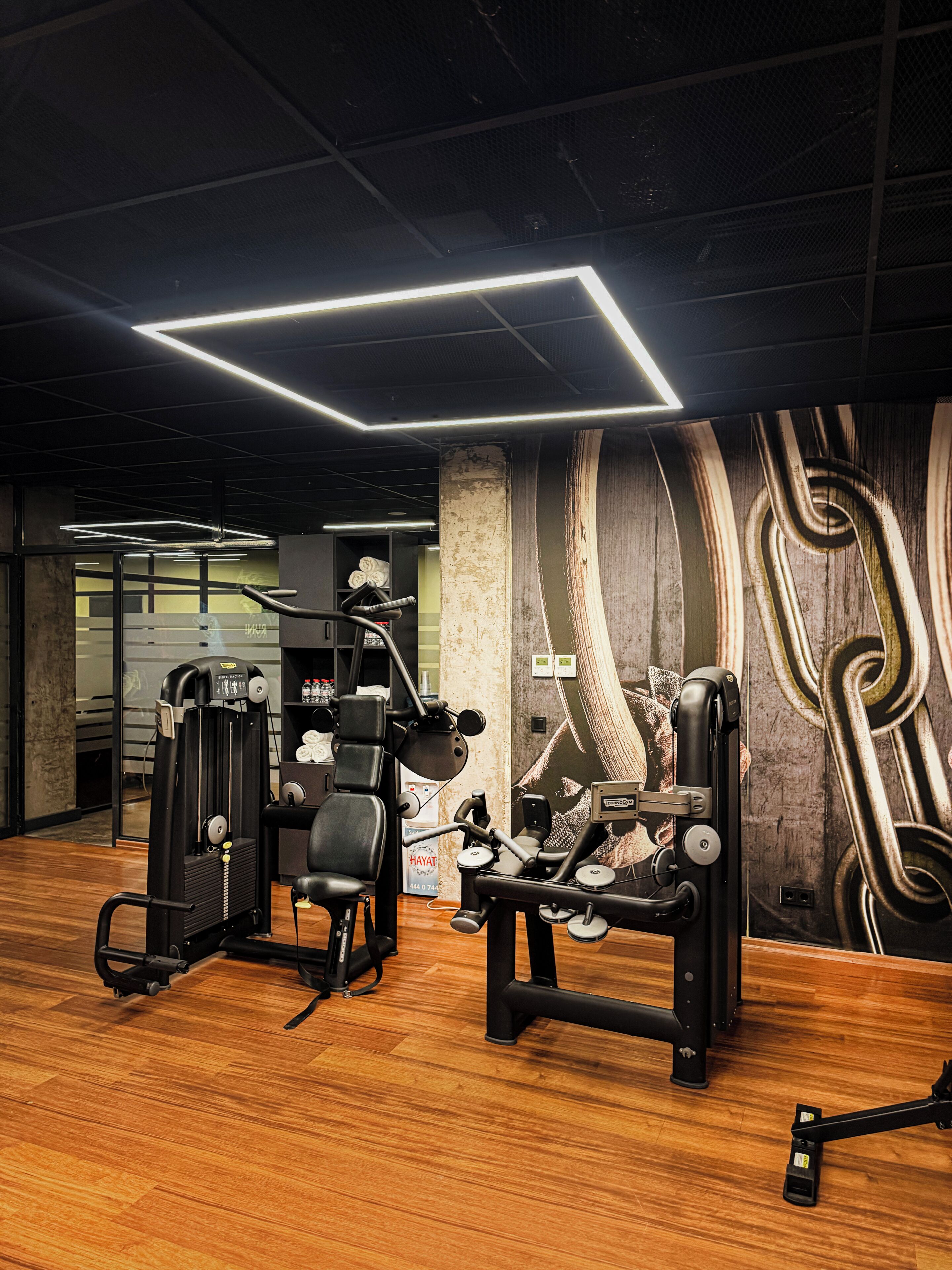 Uma academia com equipamentos de ginástica, piso de madeira e uma parede com design metálico.