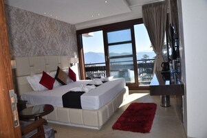 Quarto com uma cama grande, vista para as montanhas, varanda e escrivaninha com cadeira.