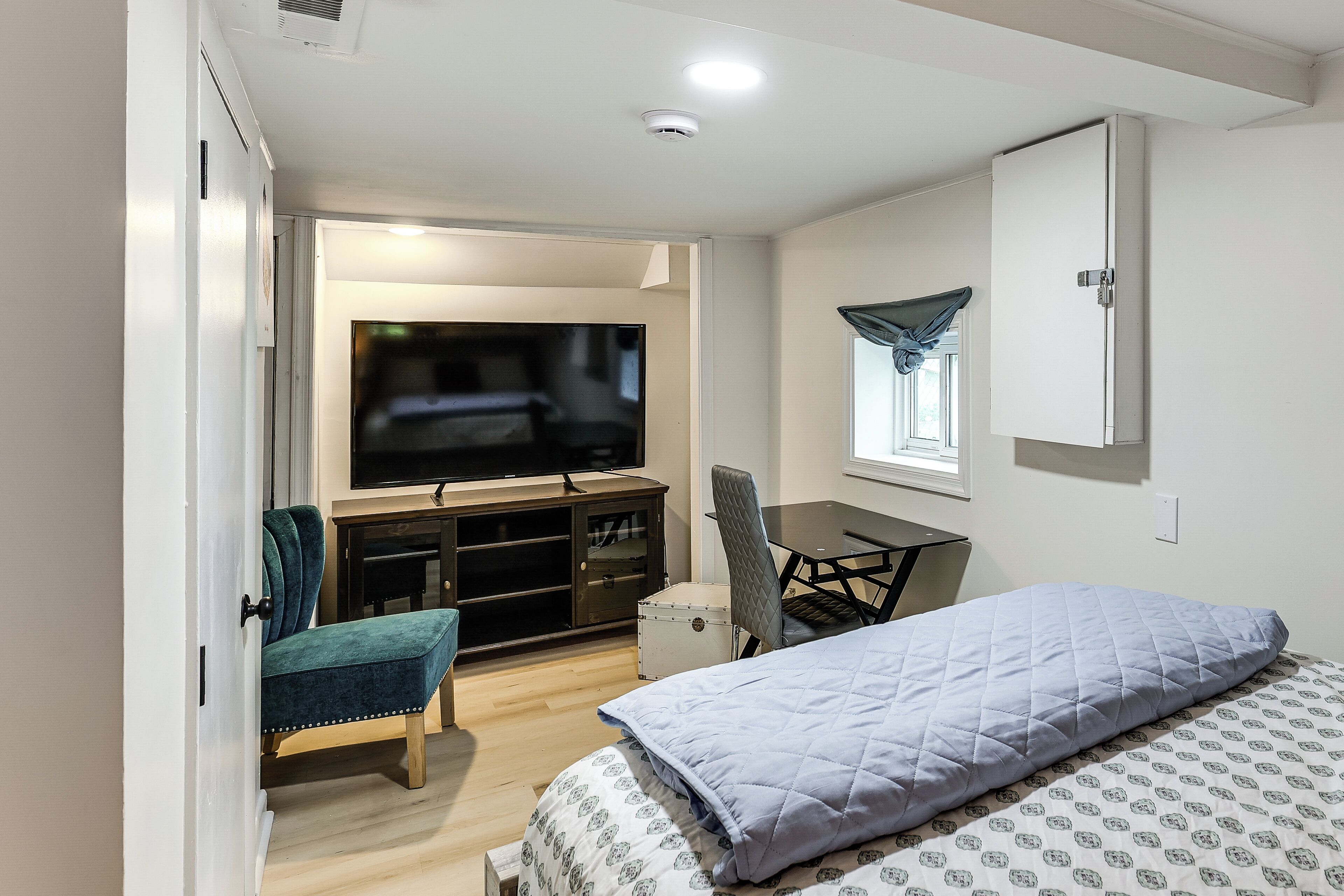 Quarto com cama, televisão, escrivaninha e cadeira.