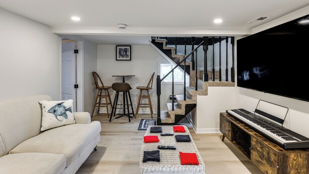 Uma sala de estar moderna com um sofá, uma mesa de centro com almofadas, um piano, uma televisão e uma escadaria que dá para outro cômodo.