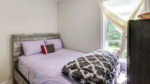 Um quarto com cabeceira de madeira, cama com colcha estampada e janela com cortinas.
