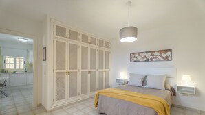 Quarto com cama, luminárias de cabeceira, obra de arte na parede e guarda-roupa com design vazado.