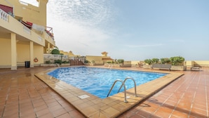 Uma piscina com deck ladrilhado, guarda-corpo branco e céu claro.