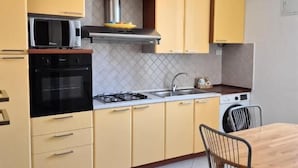 Uma cozinha compacta com armários amarelos, micro-ondas, fogão e uma área de refeições com mesa de madeira e cadeiras de metal.