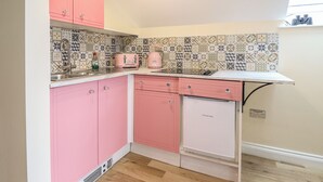 Cozinha com armários rosa, geladeira branca e azulejos de parede estampados.