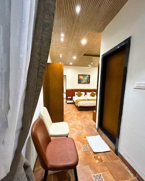 Um corredor estreito com uma cadeira, uma cama com almofadas e uma porta de madeira.