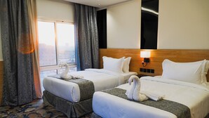 Quarto de hotel com duas camas, uma janela grande e vista para a cidade.