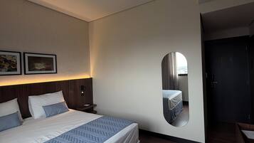 Quarto de hotel com uma cama, um espelho, chão de madeira e uma porta.