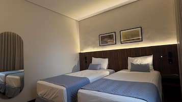 Quarto de hotel com duas camas, um espelho grande e duas imagens emolduradas na parede.